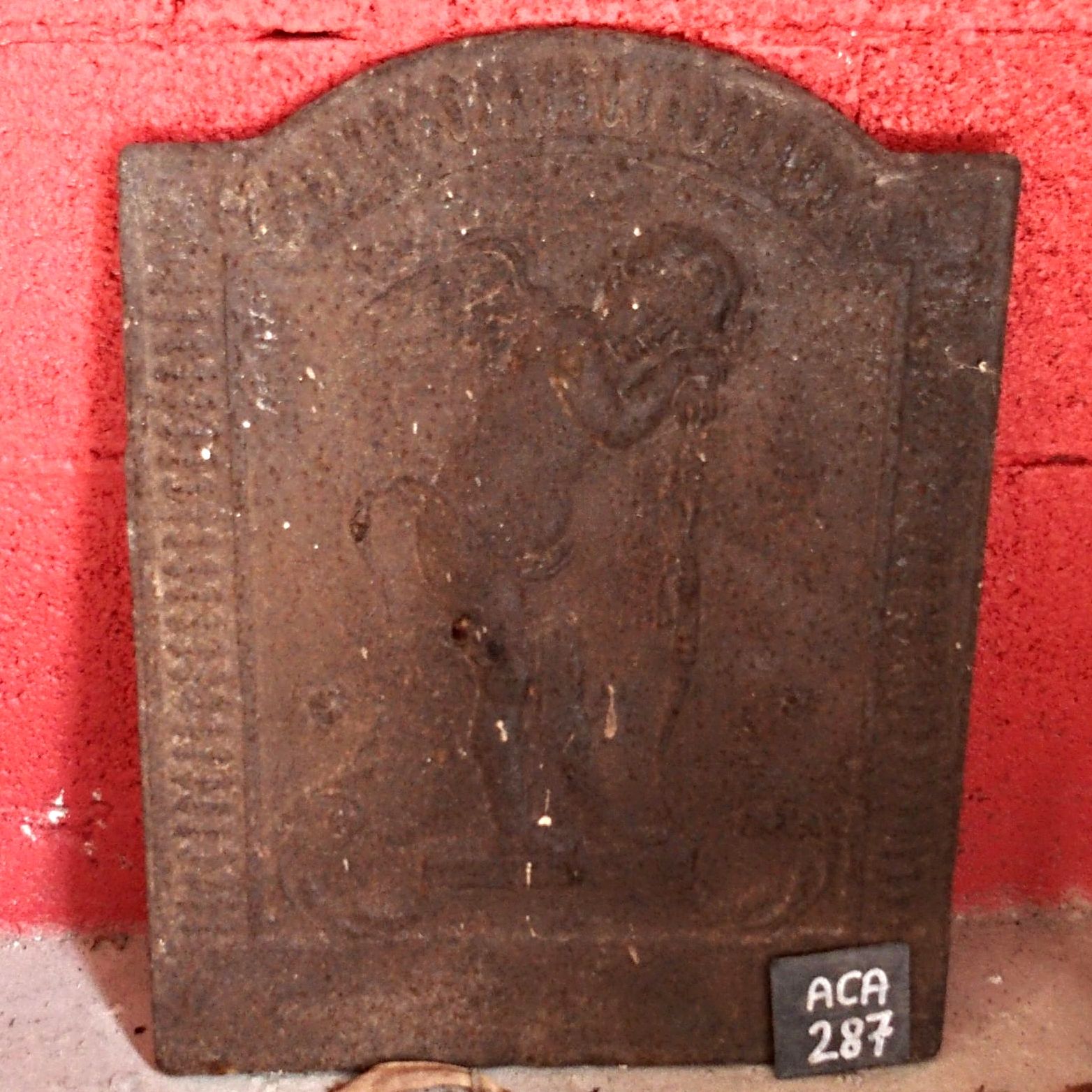 Cast fireback decorated with cherub and bow ǀ Fireplace accessories.