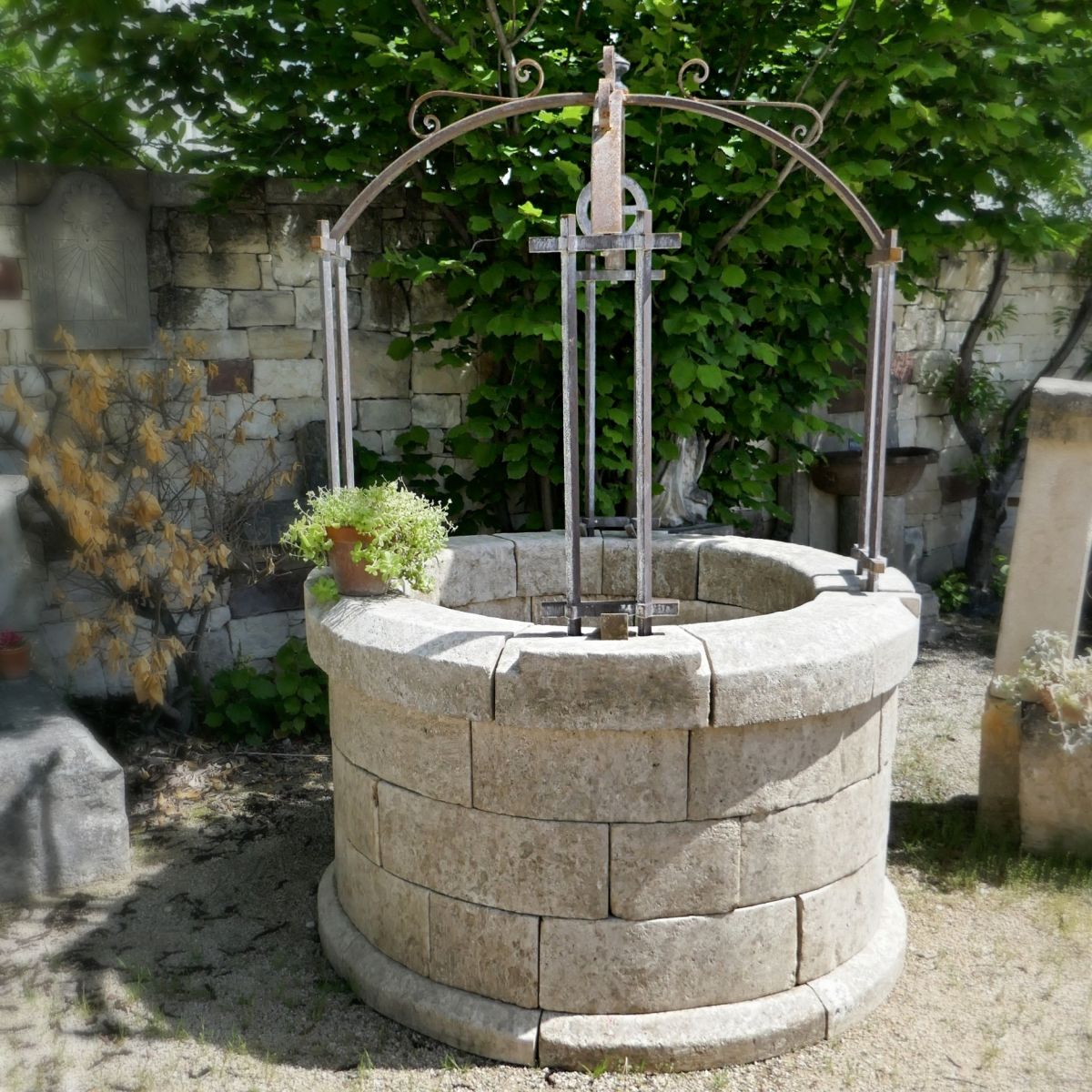 Puits rond en pierre et son haut de puits en fer forgé avec poulie