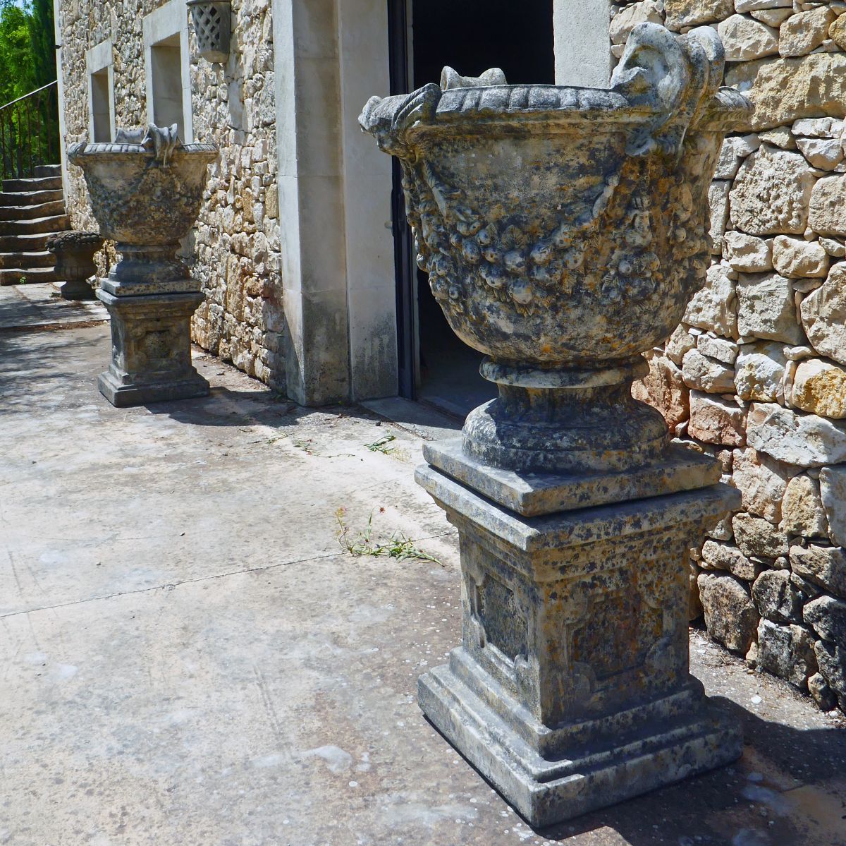 Pair of weathered composite stone large vases on paneled pedestals